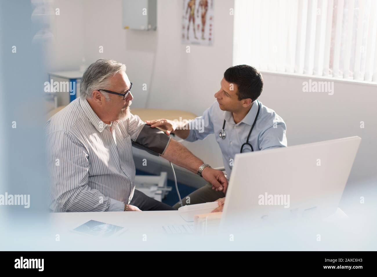 Male doctor checking blood pressure of senior patient in doctors office ...