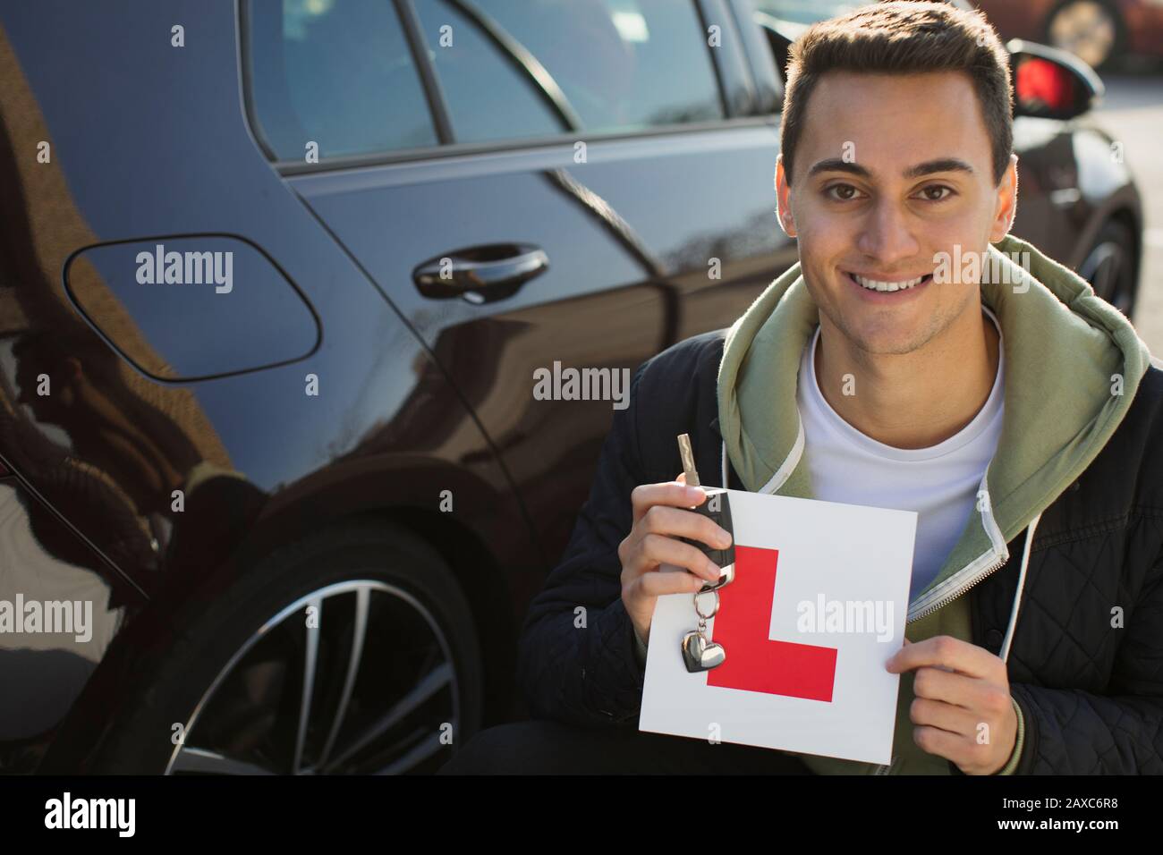 Portrait confident, happy young man holding learners permit by car ...