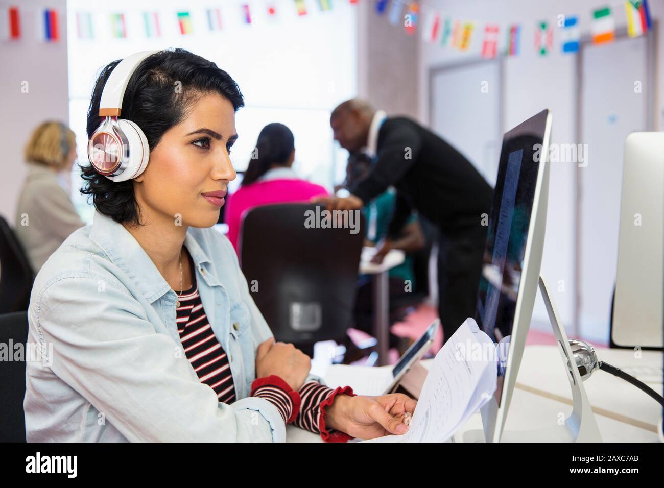Focused female community college student with headphones using computer ...