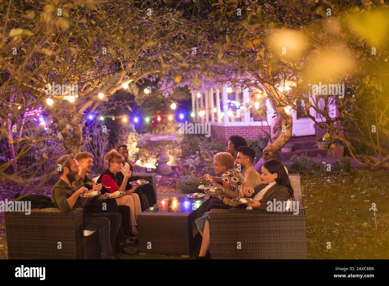 Friends talking and eating dessert under trees with string lights at ...