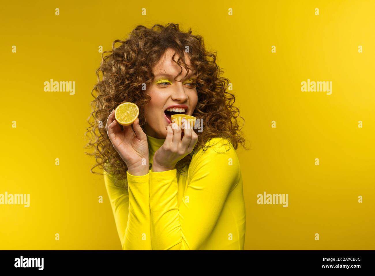 Young beautiful smiling women with curly hair tasting sour lemon halves ...