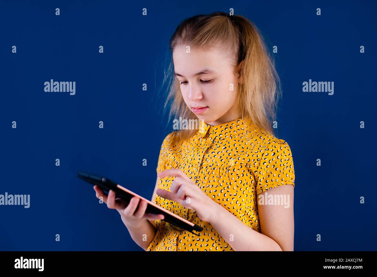 Blonde teenage girl playing with tablet pc on blue background ...