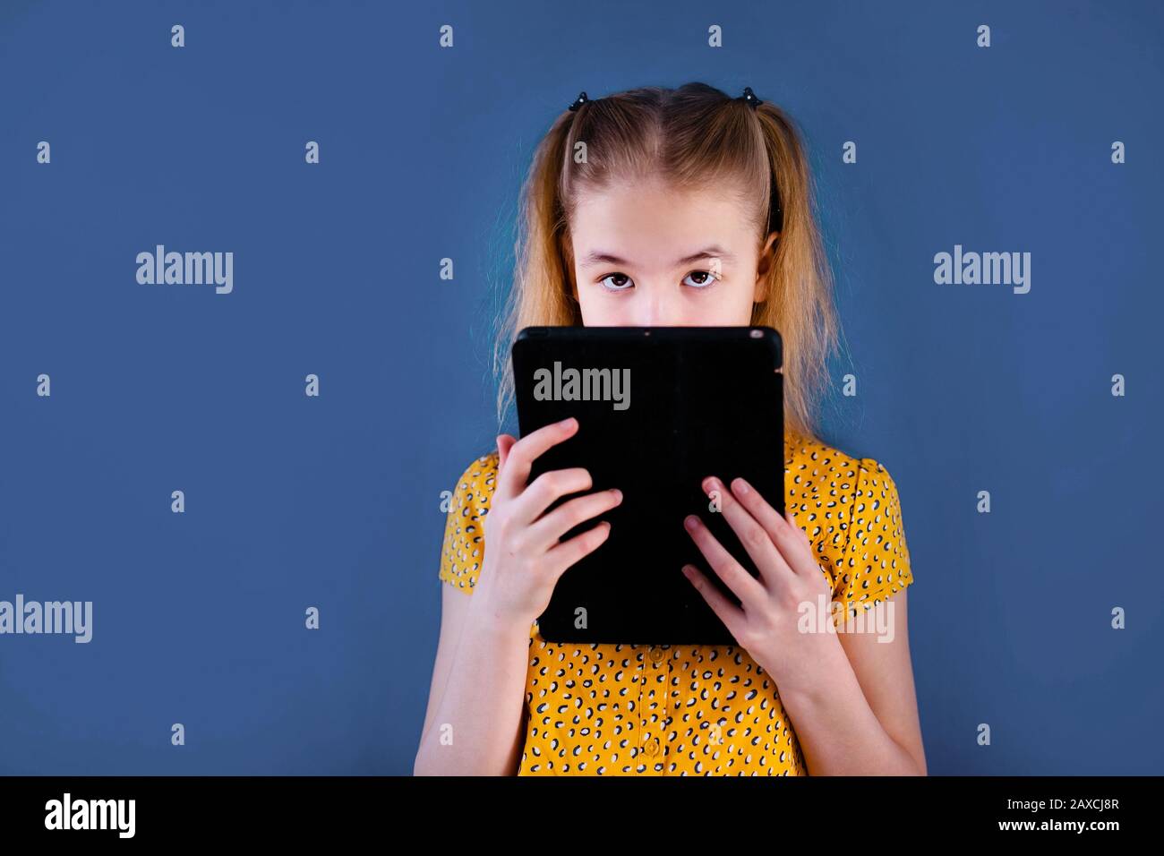 Blonde teenage girl playing with tablet pc on blue background ...
