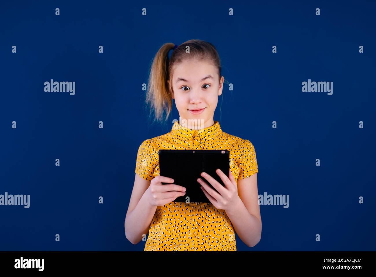 Blonde teenage girl playing with tablet pc on blue background ...