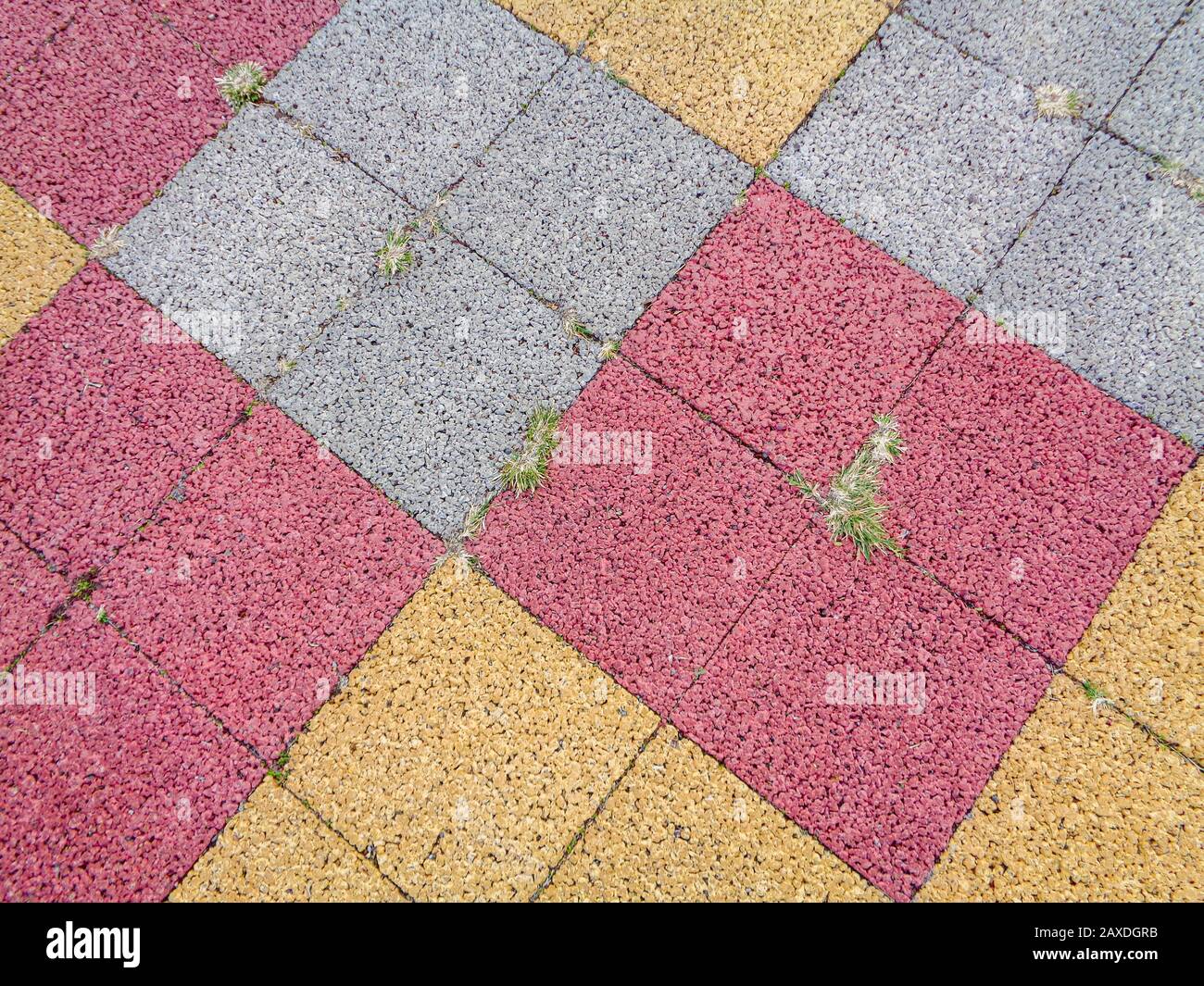 Colourful paving slabs with tufts of grass growing out of the cracks ...