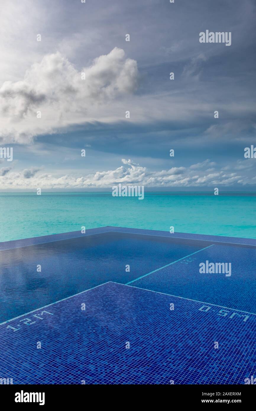 A brilliant blue infinity swimming pool beside the turquoise sea with ...