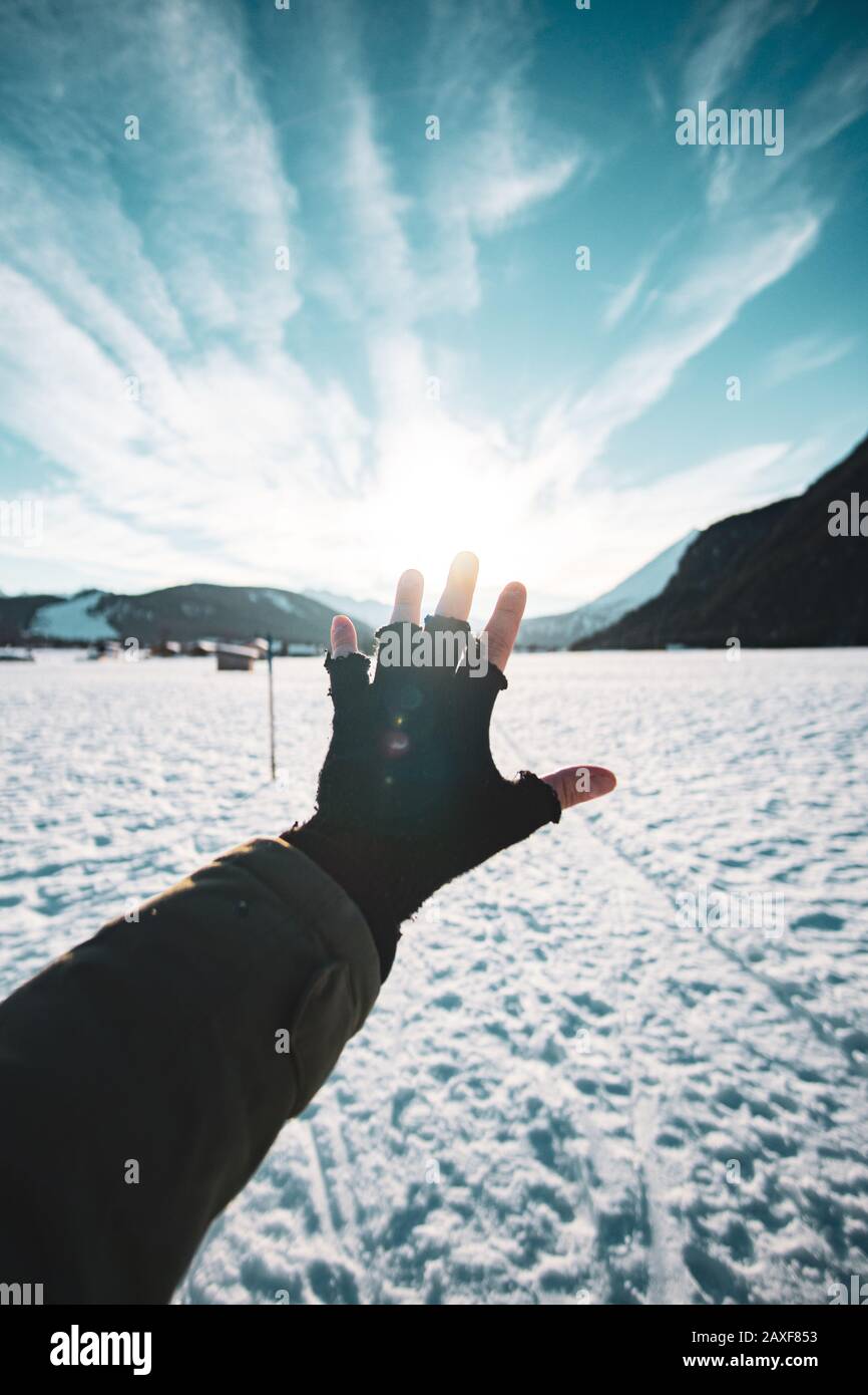 Hand wearing gloves in front of the rising sun and a cloudy blue sky in ...