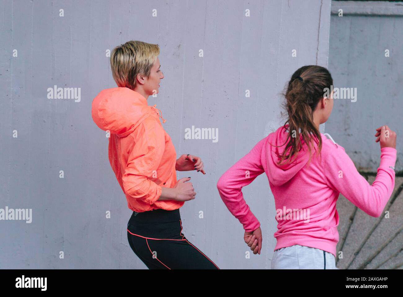Attractive athletic girls running along urban gray wall buildings ...