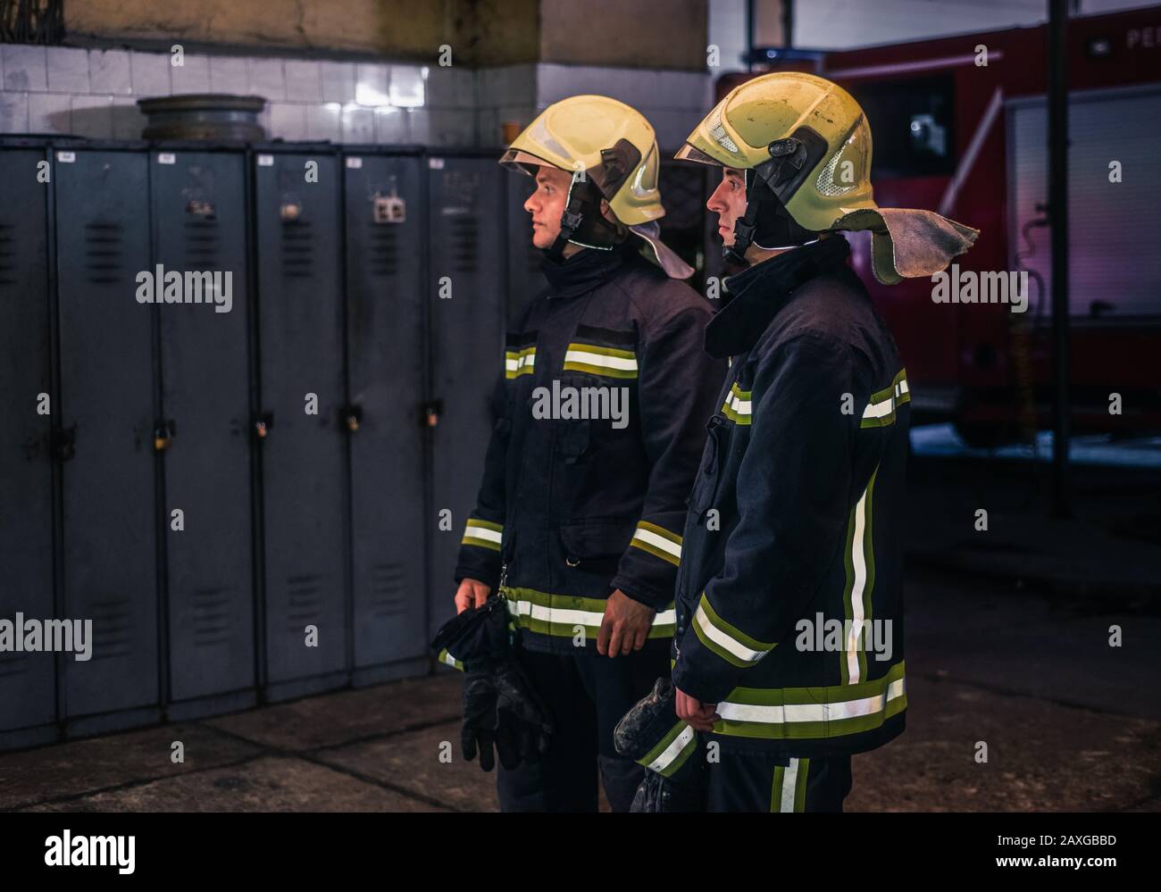 Portrait of two young firemen in uniform standing inside the fire ...