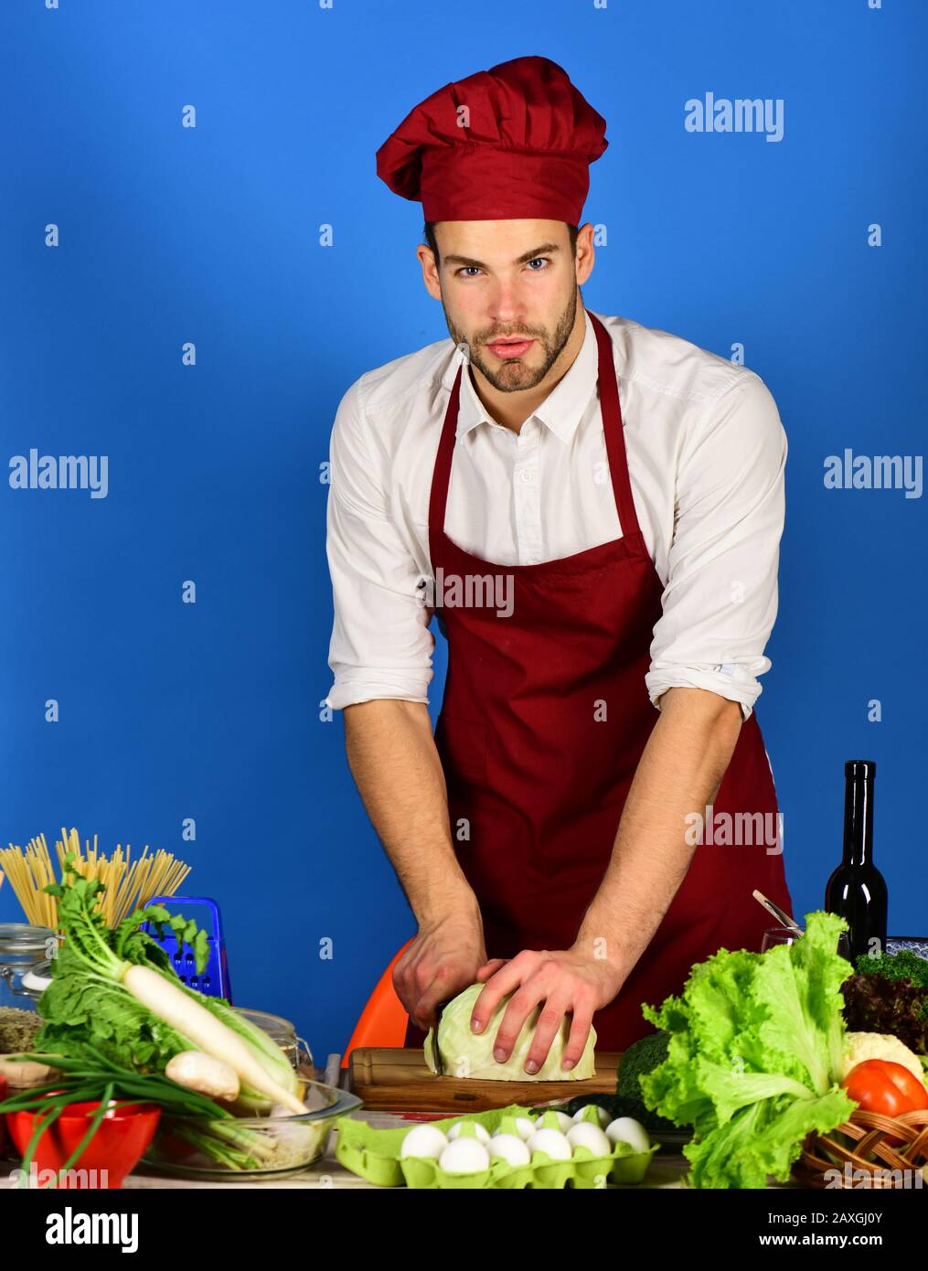 Cook works in kitchen near table with vegetables and tools. Chef with ...
