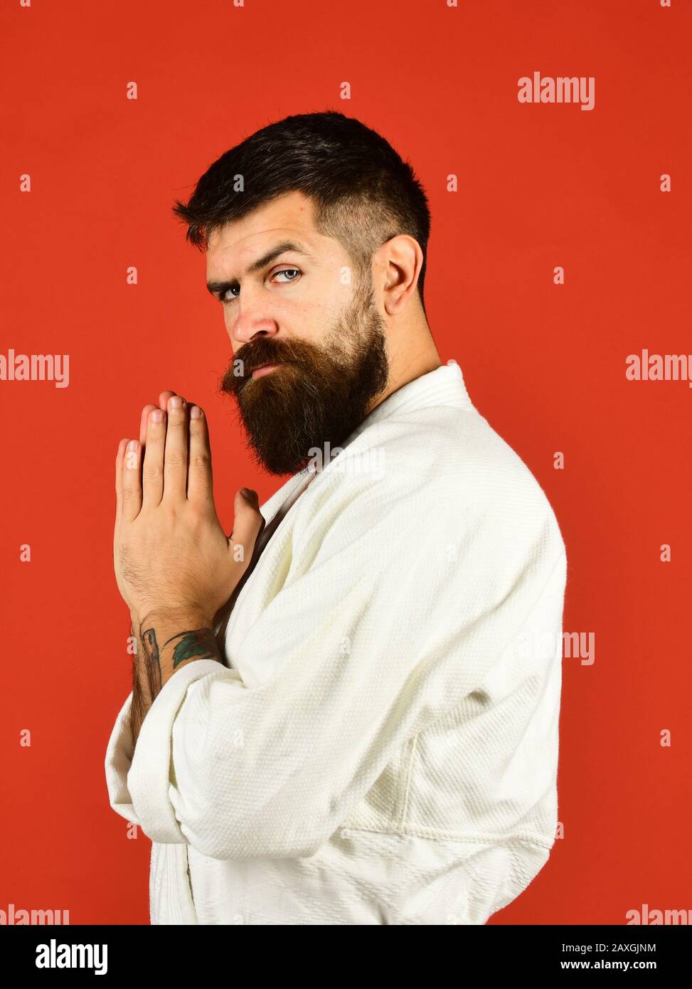 Man with beard in white kimono on red background. Training and combat ...