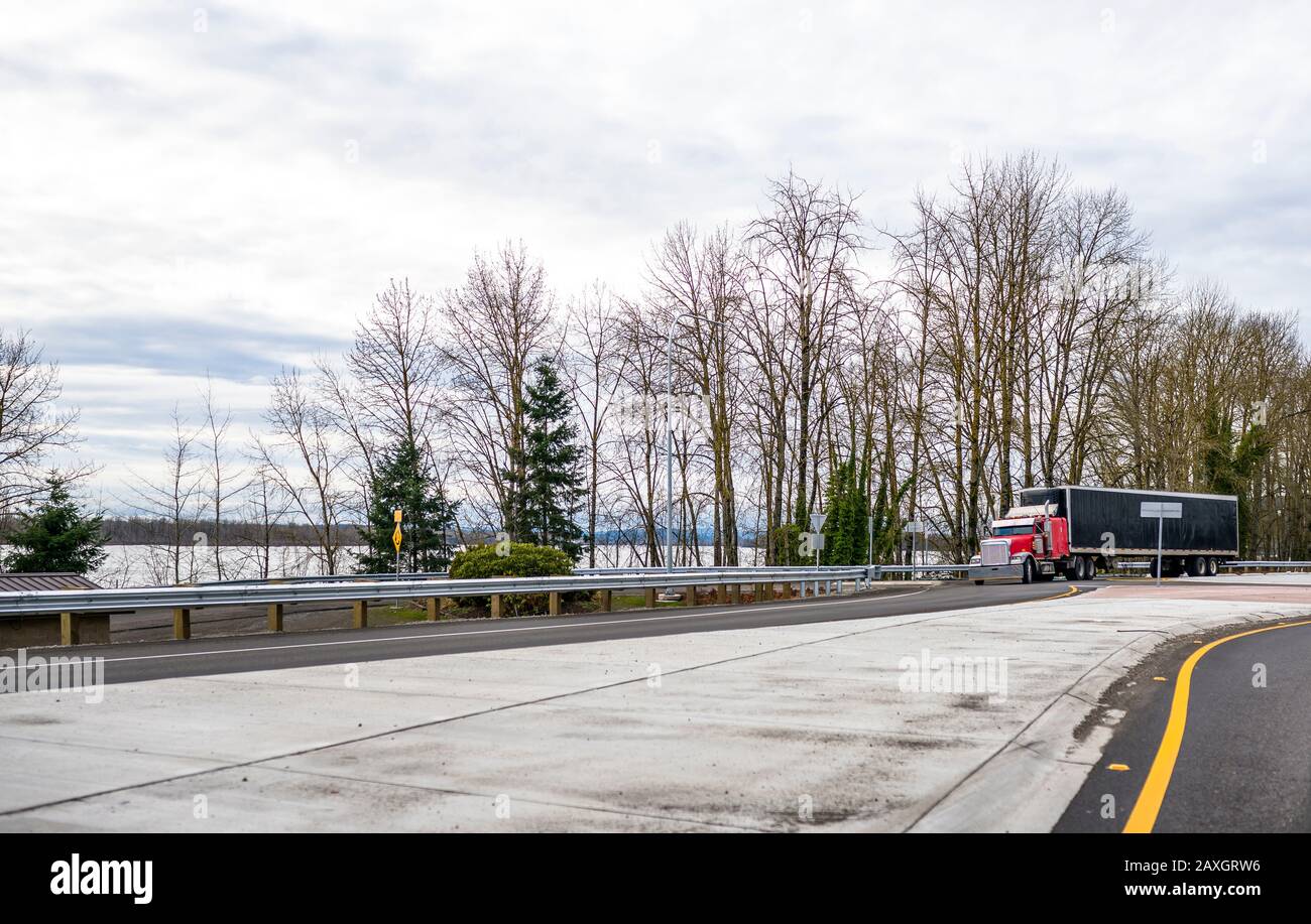 Red classic big rig semi truck with covered black semi trailer turning ...