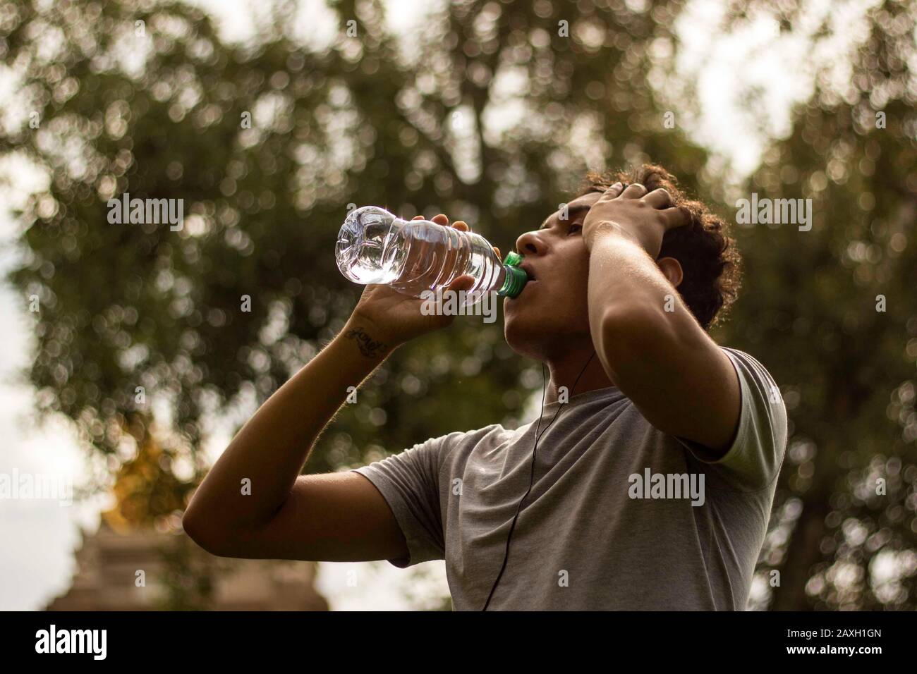 Runner drinking water. Exhausted latin young man with bottled water ...