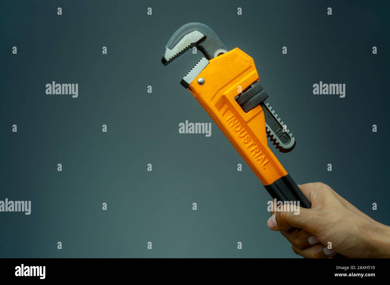 Plumber hand holding handle of chrome pipe wrench isolated on dark ...