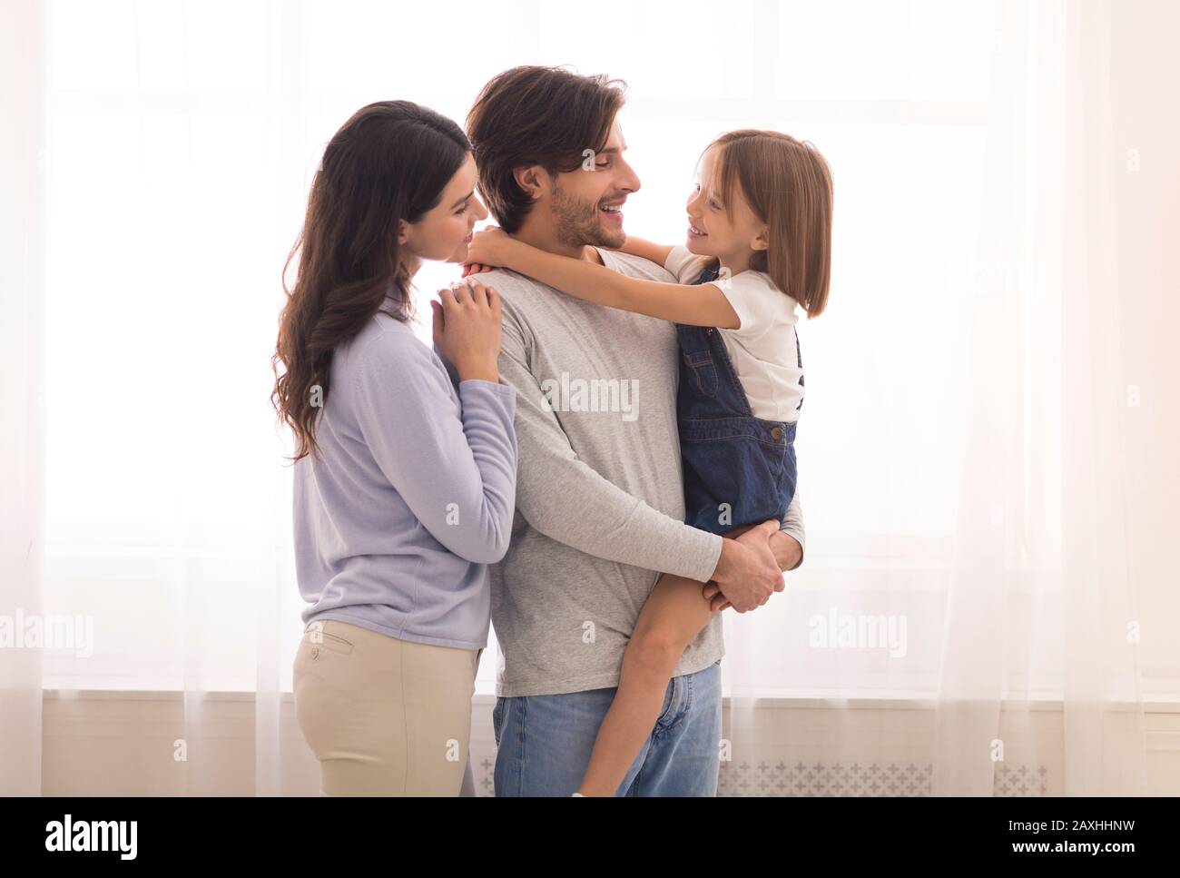 Affectionate family of three embracing near window at home Stock Photo ...