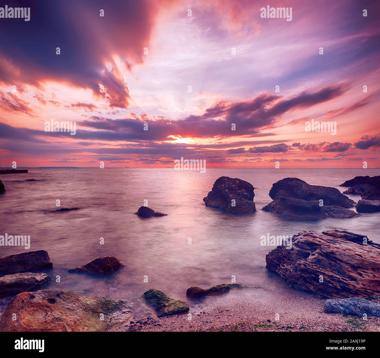 Beautiful colorful sunrise at the sea with dramatic clouds and boulders ...