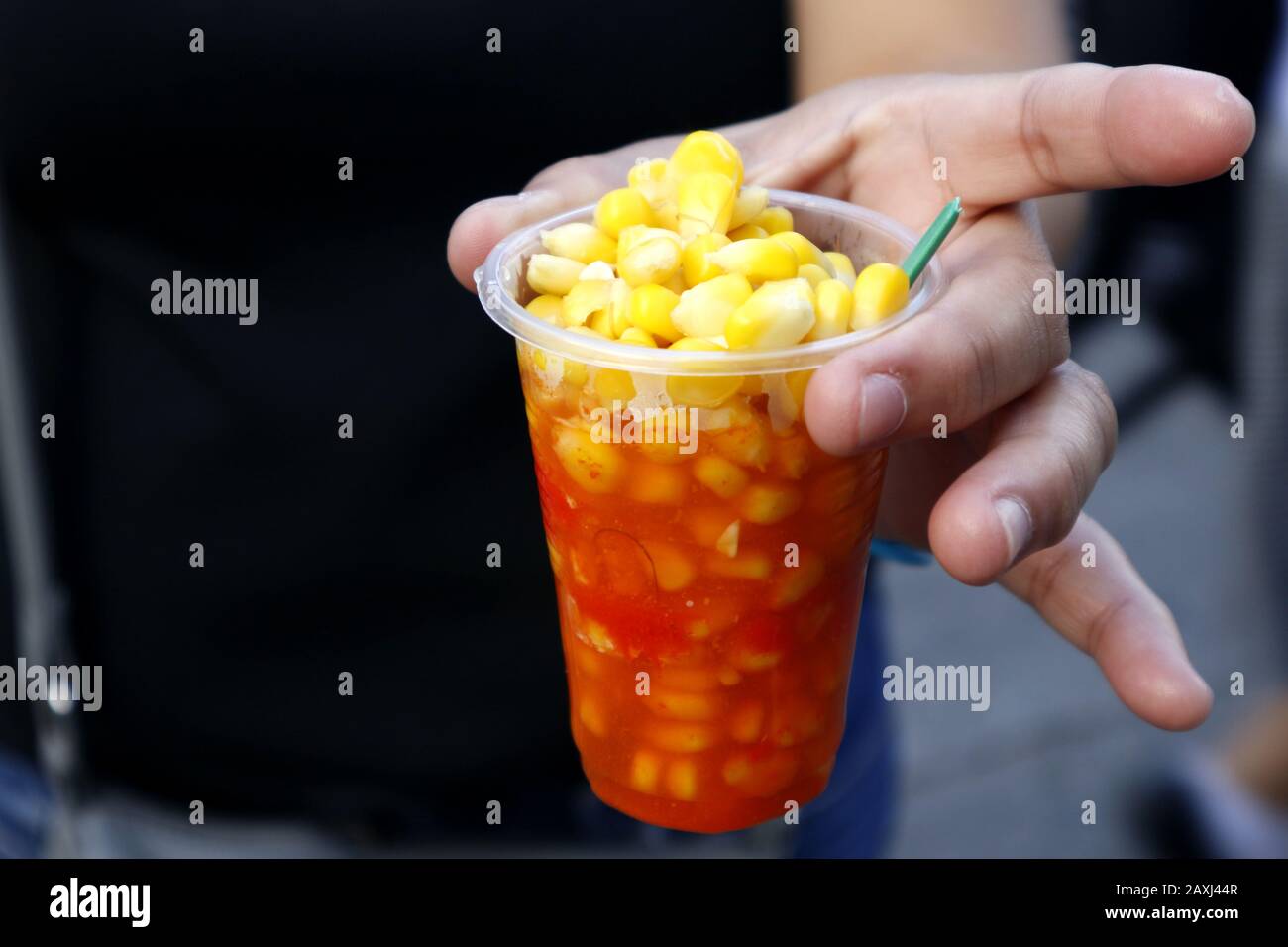 Photo of a hand holding a steamed corn with cheese in a plastic cup ...