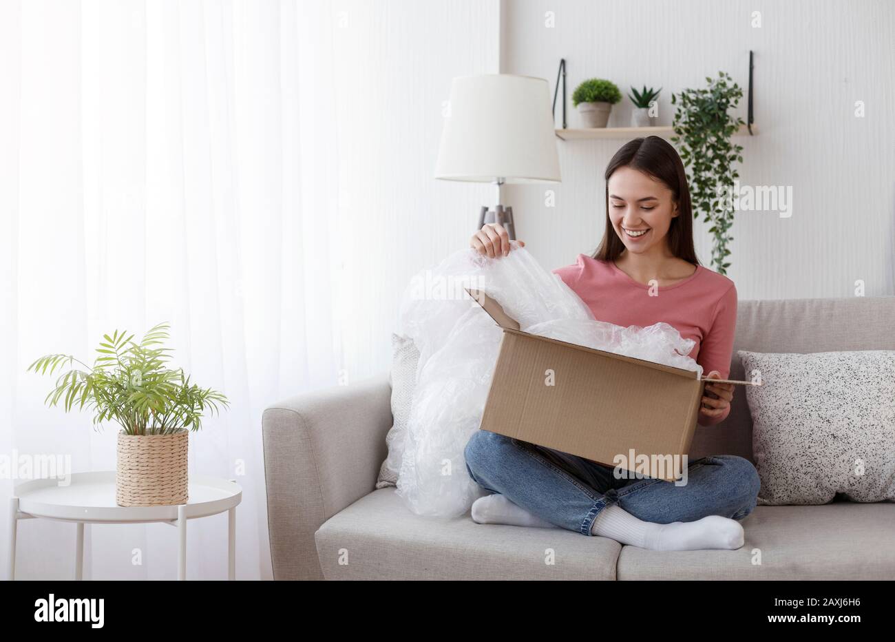 Excited young woman unwrapping parcel, buying goods via internet Stock ...