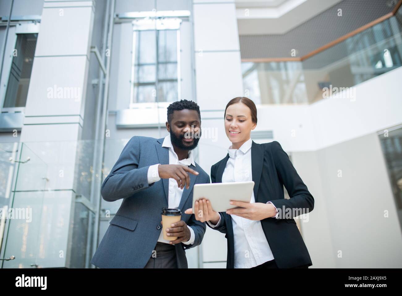Positive Black manager with coffee cup pointing at tablet while ...