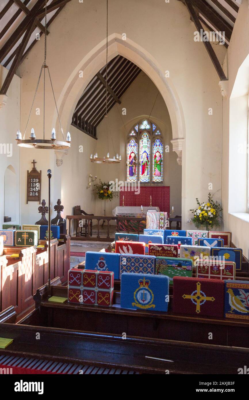 Knitted woollen pew kneelers rest wooden pews, view towards altar and ...