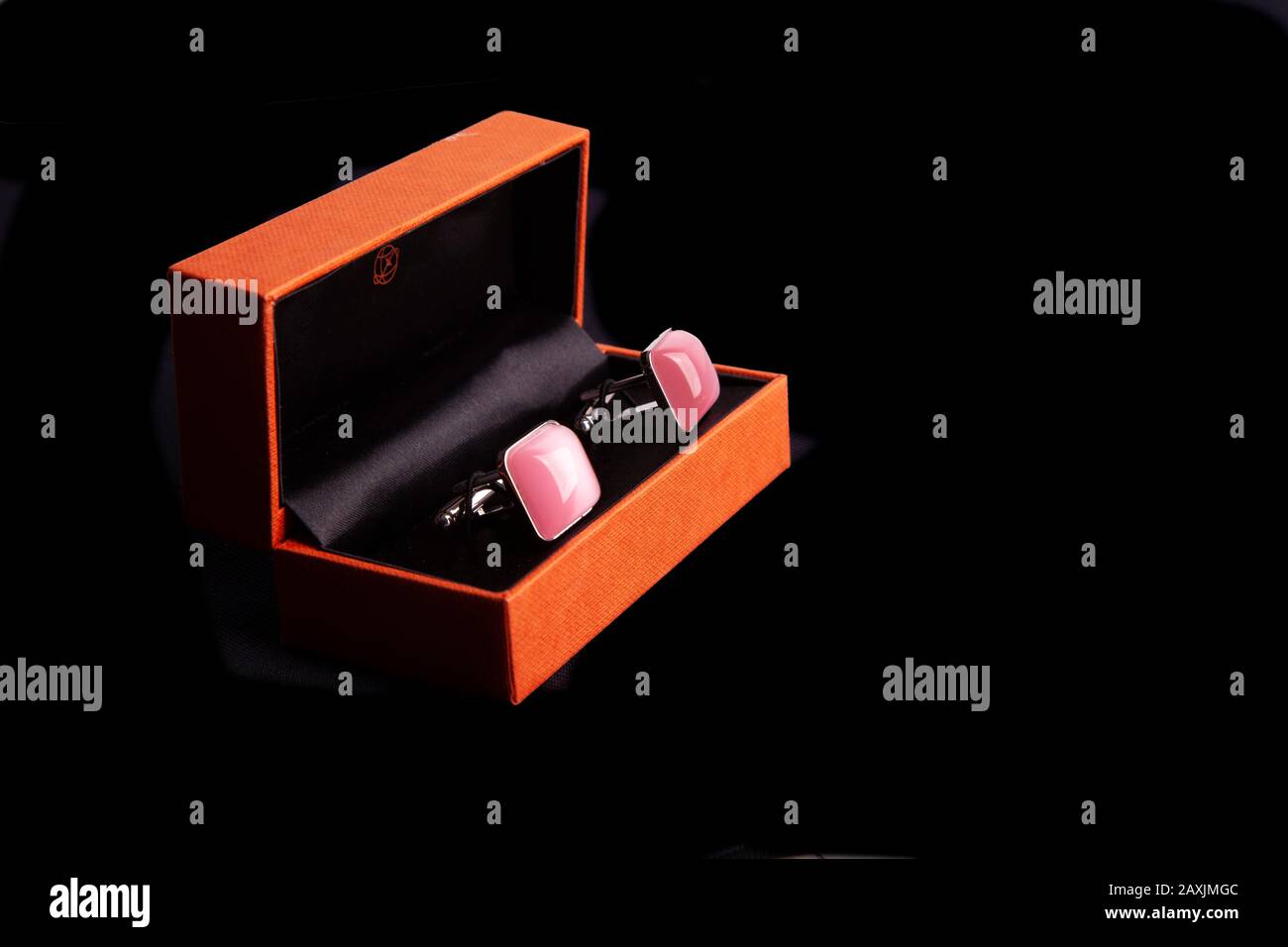 Pink stoned cuff links in a orange box on display on a Black background ...