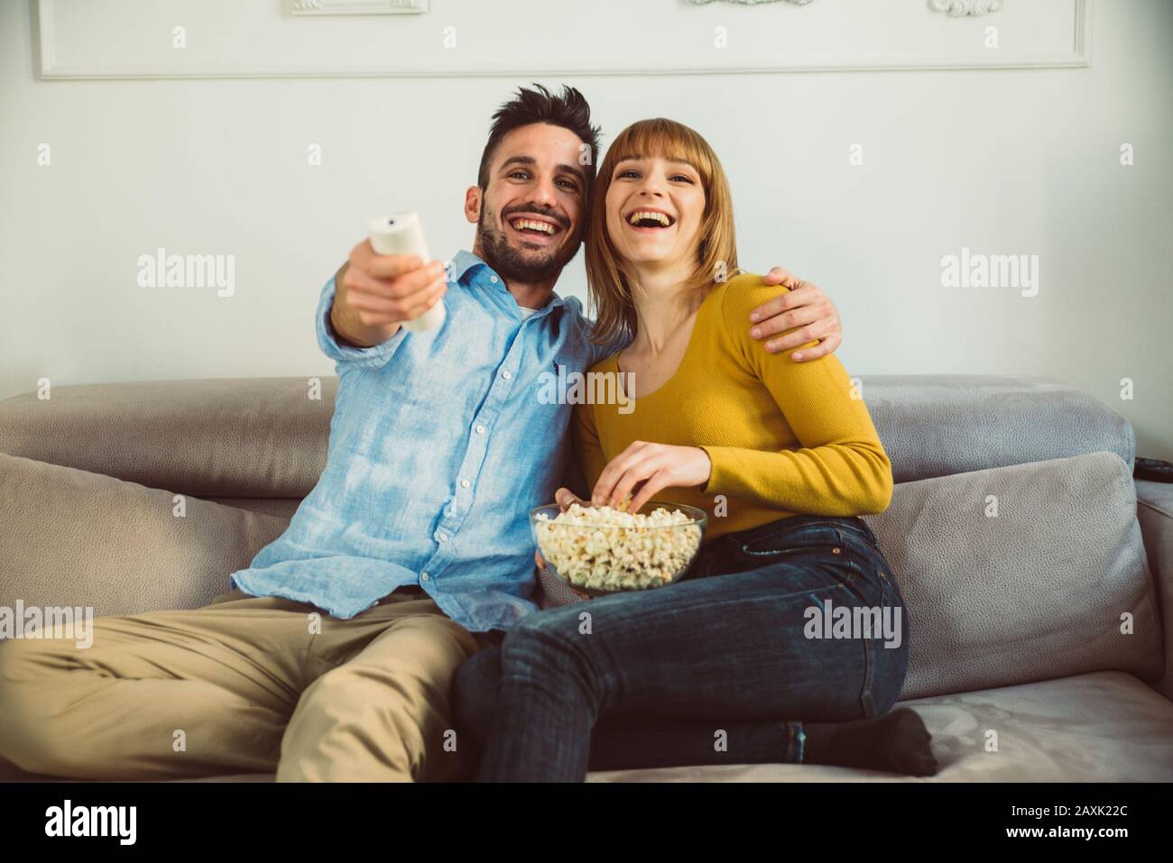 Happy beautiful couple having fun watching TV and eating pop corn at ...