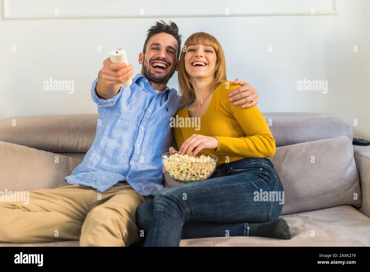 Happy beautiful couple having fun watching TV and eating pop corn at ...