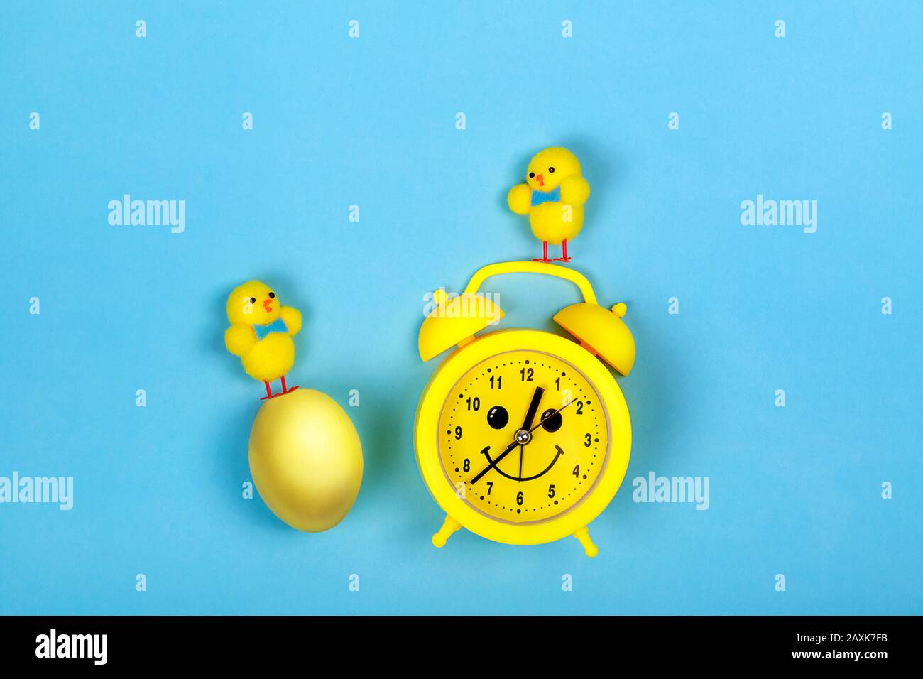 Retro yellow alarm clock with drawn smiling face and toys chicken and ...