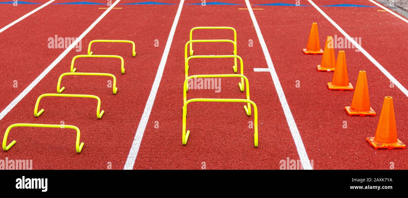 Yellow mini bannana hurdles and orange cones set up in lanes on a red track for speed and ...