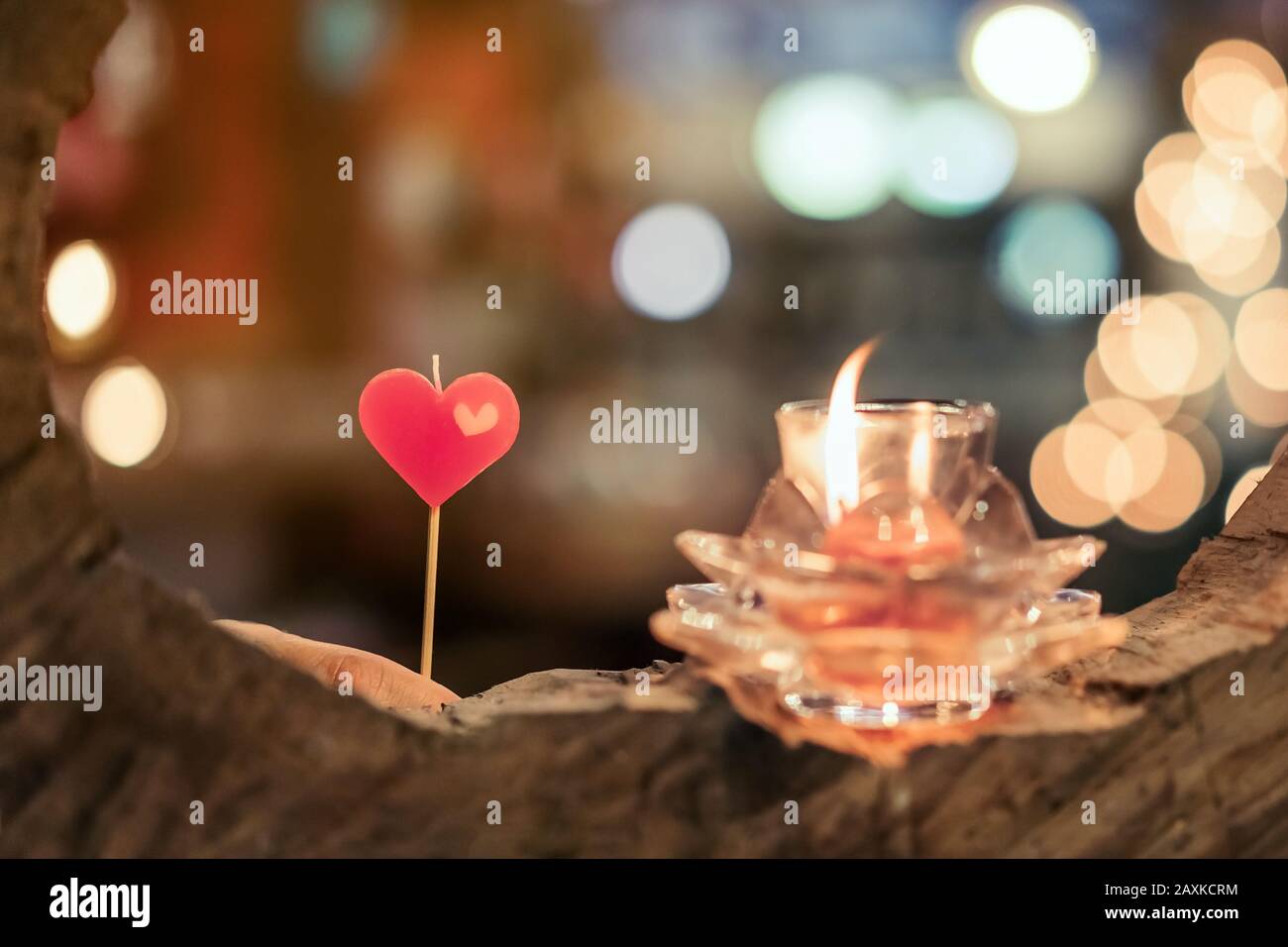 A red heart shaped candle and candlelight in small glass cup to ...