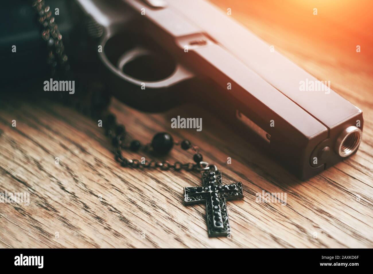 On a wooden table lies an airsoft black pistol and a black Gothic cross ...