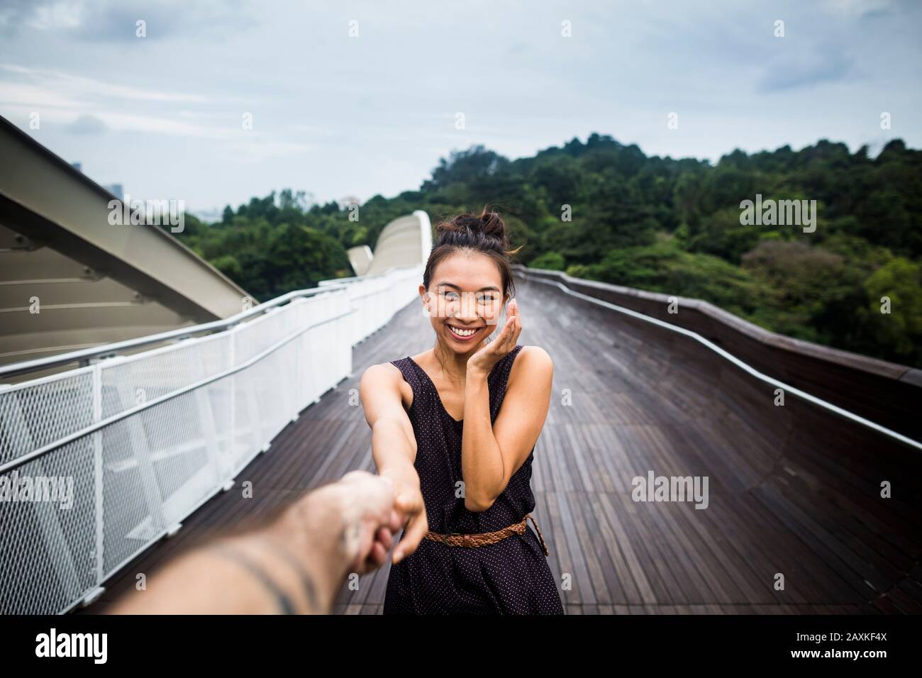 Smiling young woman standing on a bridge, holding man's hand Stock ...