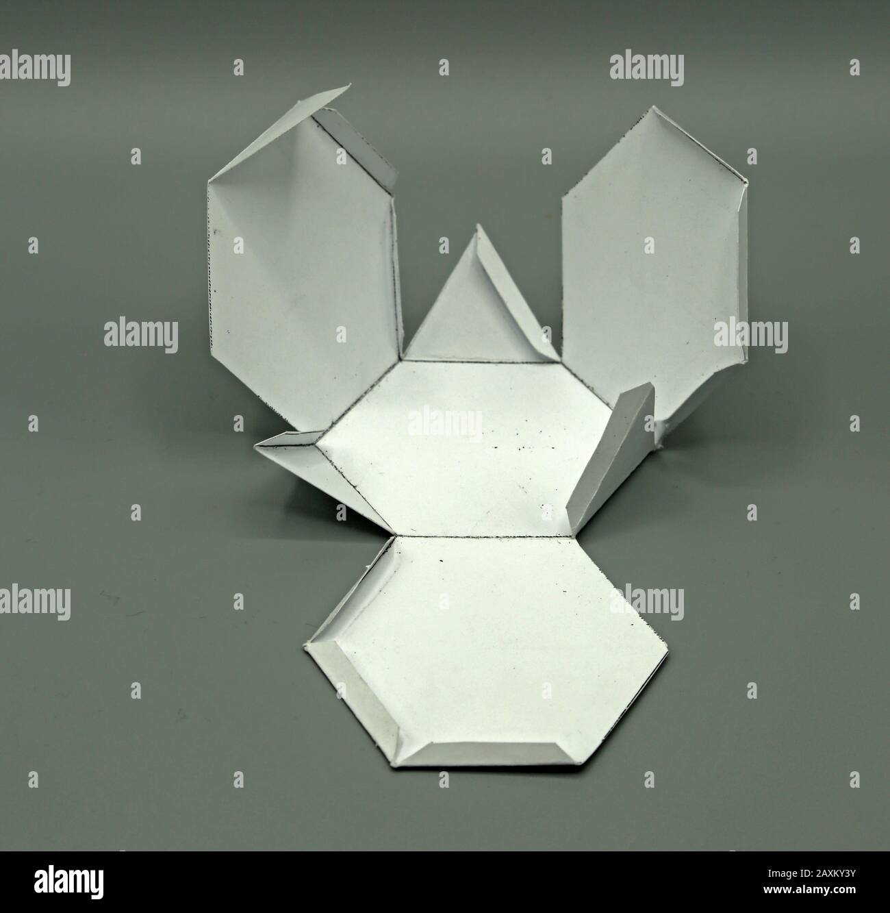 Geometric shape cut out of paper and photographed on grey background ...