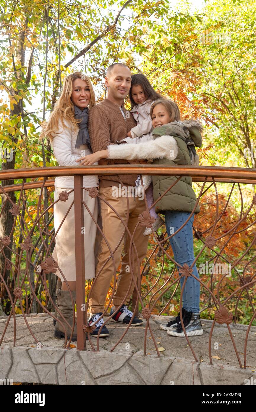 Cheerful daughters hugging beautiful parents while standing on bridge ...