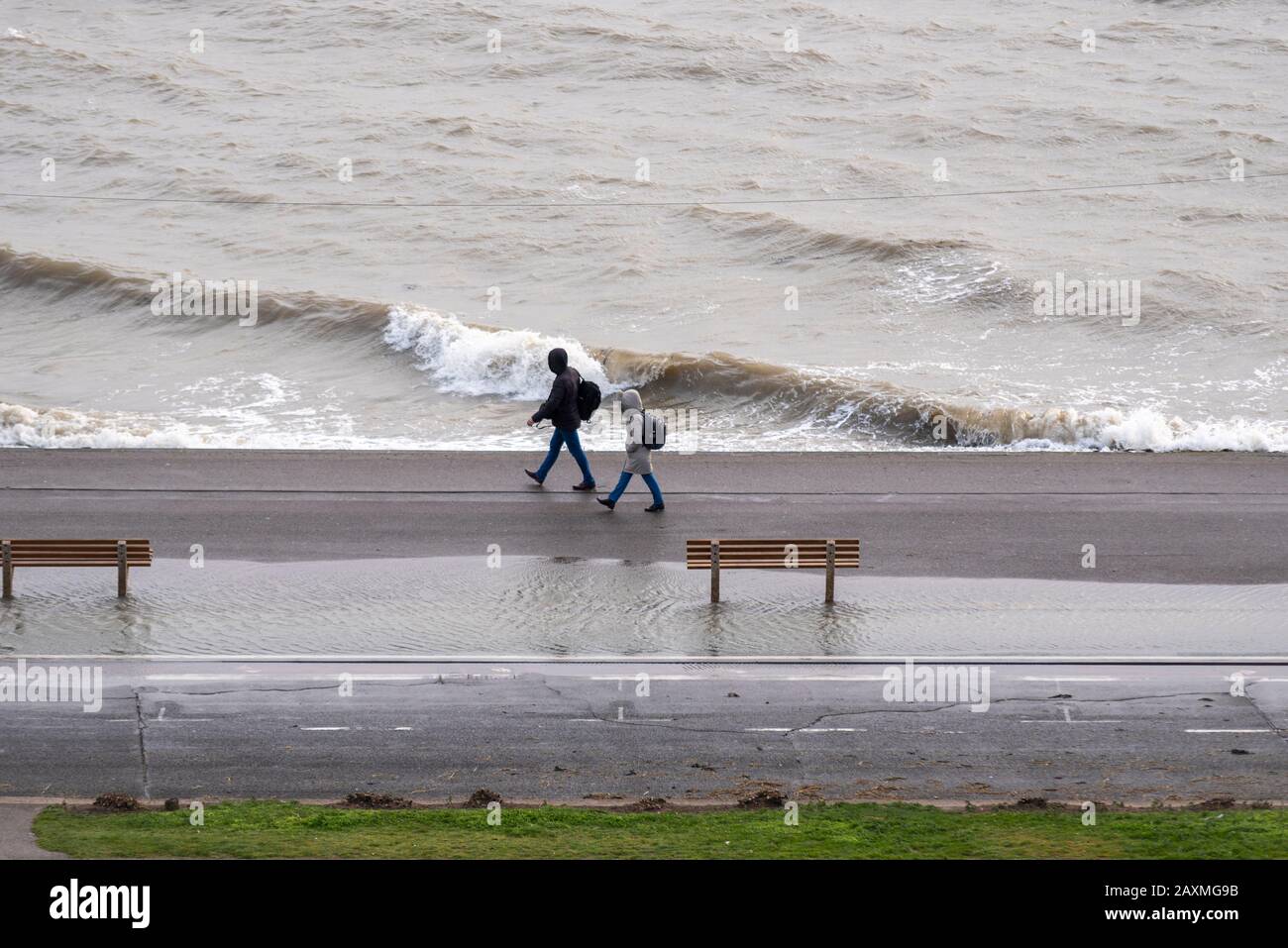 Two people walking the seafront promenade with flooding during the high ...