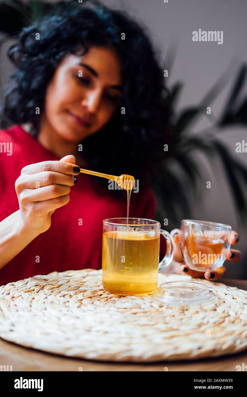 Brunette woman sweetening a tea with honey Stock Photo - Alamy