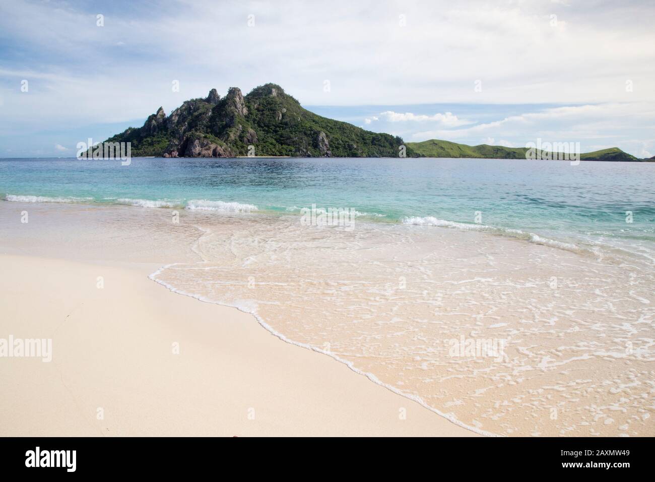 Smooth sandy beach with blue waters and tropical island in background ...