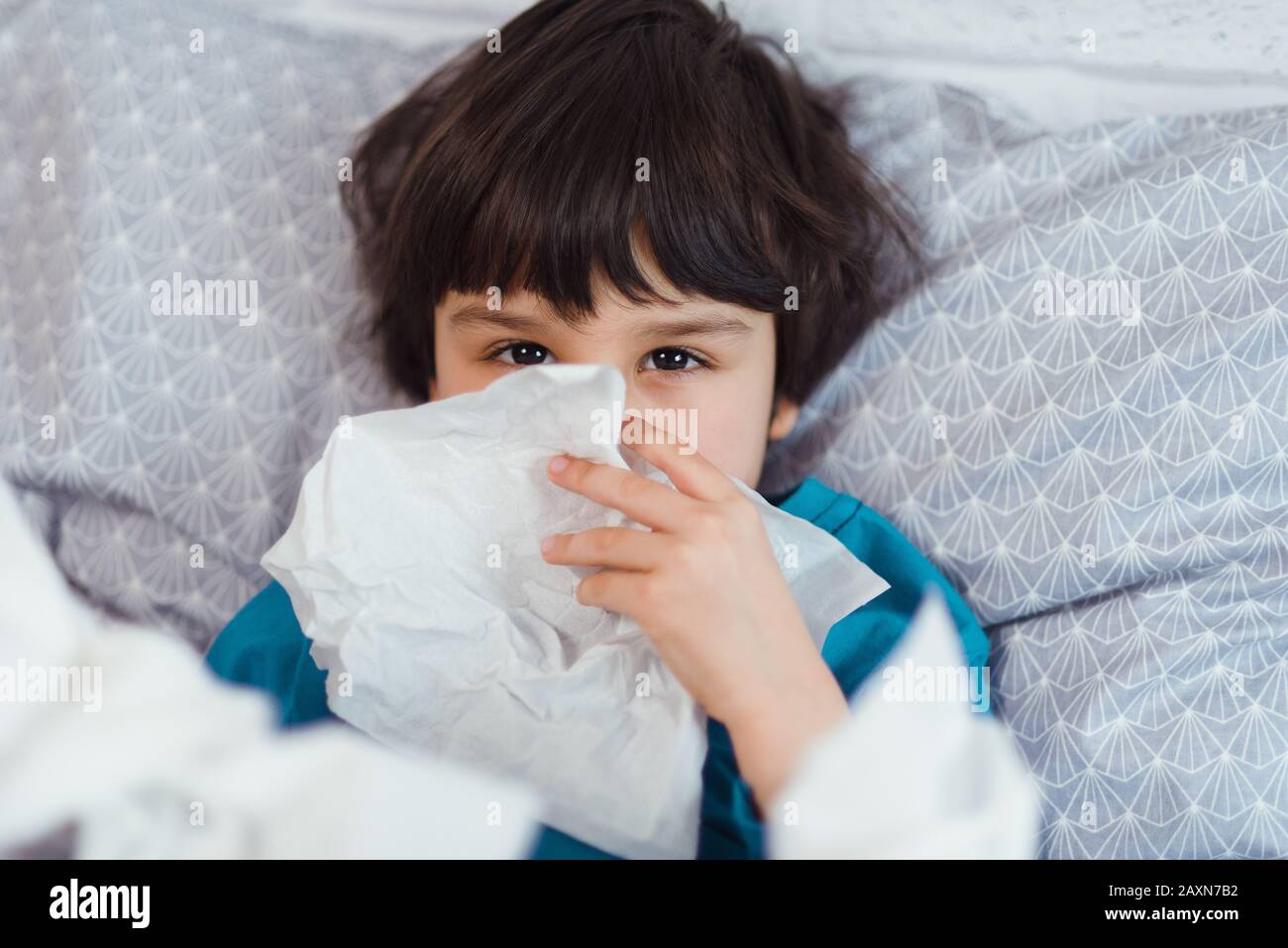 Little child boy blow his nose. Sick child with napkin in bed. Allergic ...
