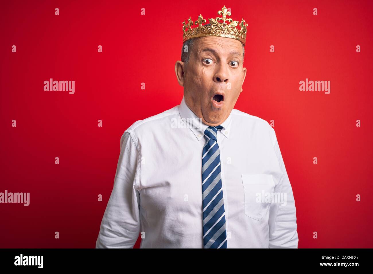 Senior handsome businessman wearing king crown standing over isolated ...