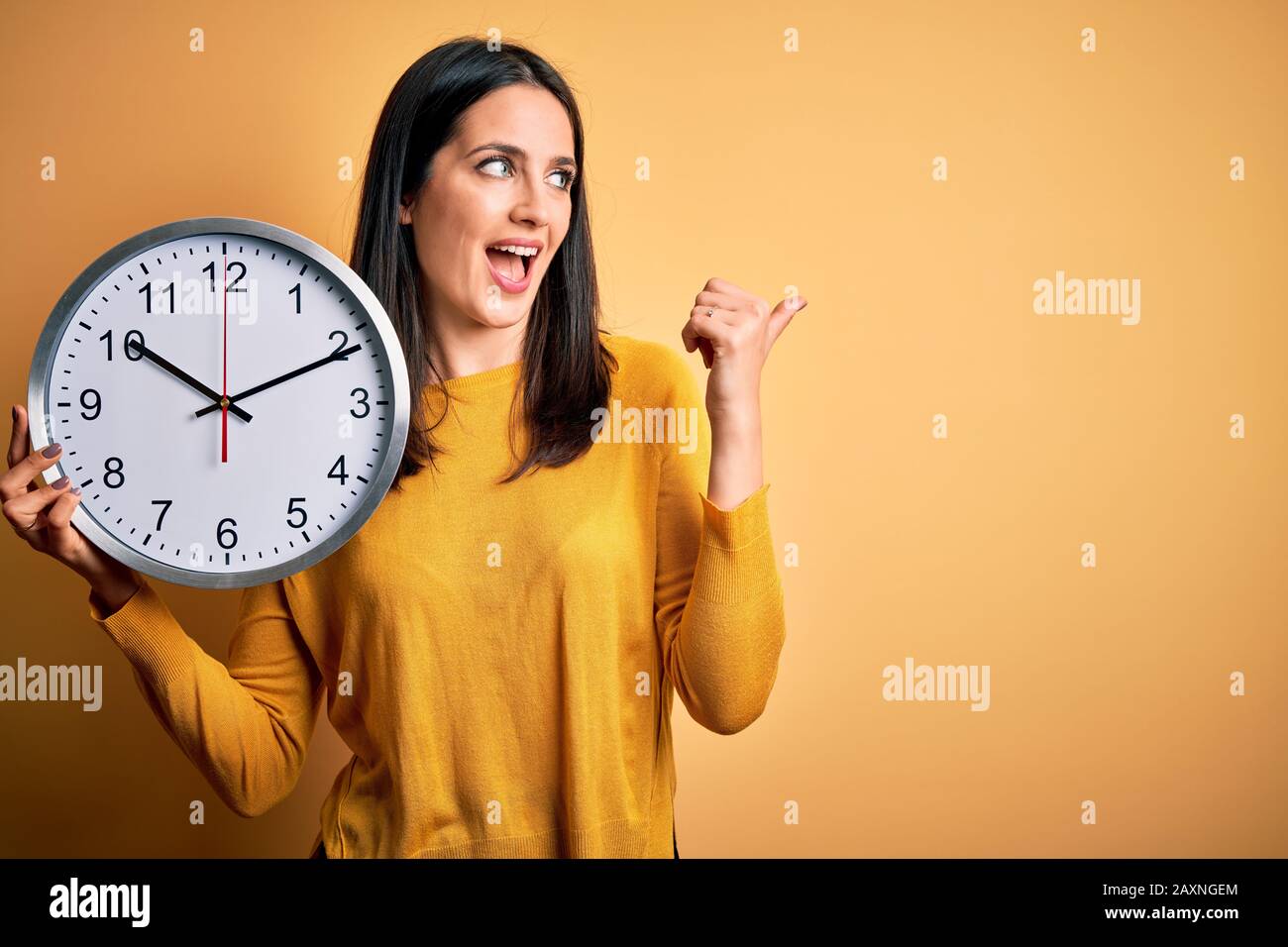 Young woman with blue eyes doing countdown holding big clock over ...