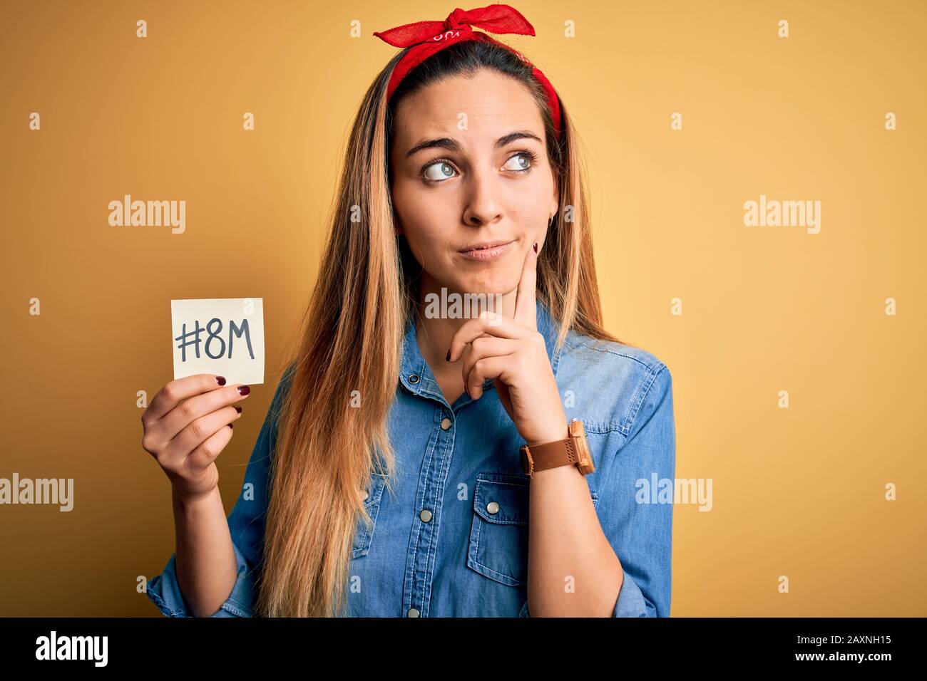 Beautiful woman with blue eyes celebrating 8th march womens day holding reminder paper serious ...