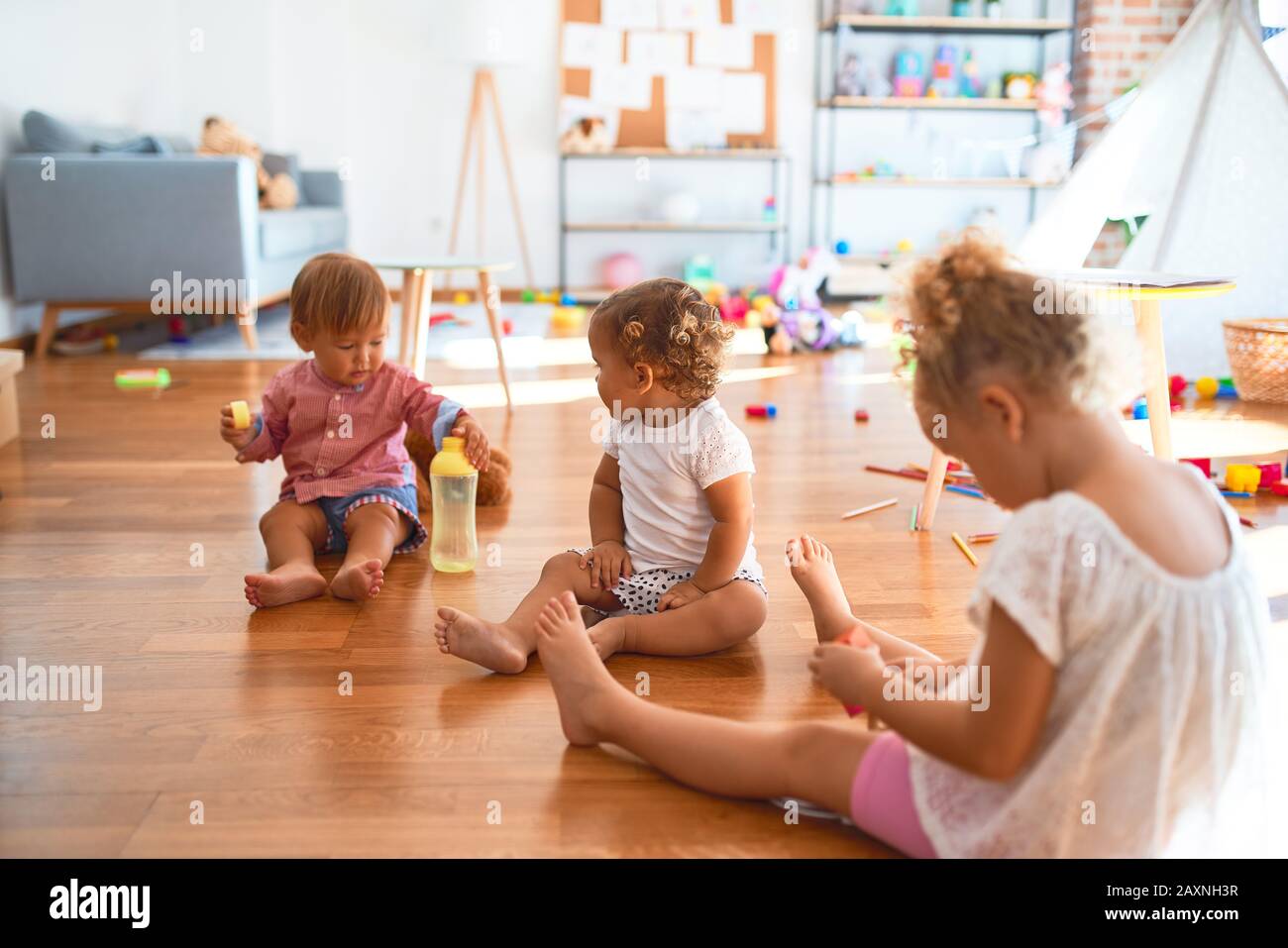 Adorable toddlers sitting on the floor playing around lots of toys at ...