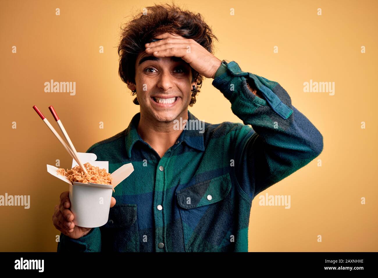 Young handsome man eating noodles standing over isolated yellow ...