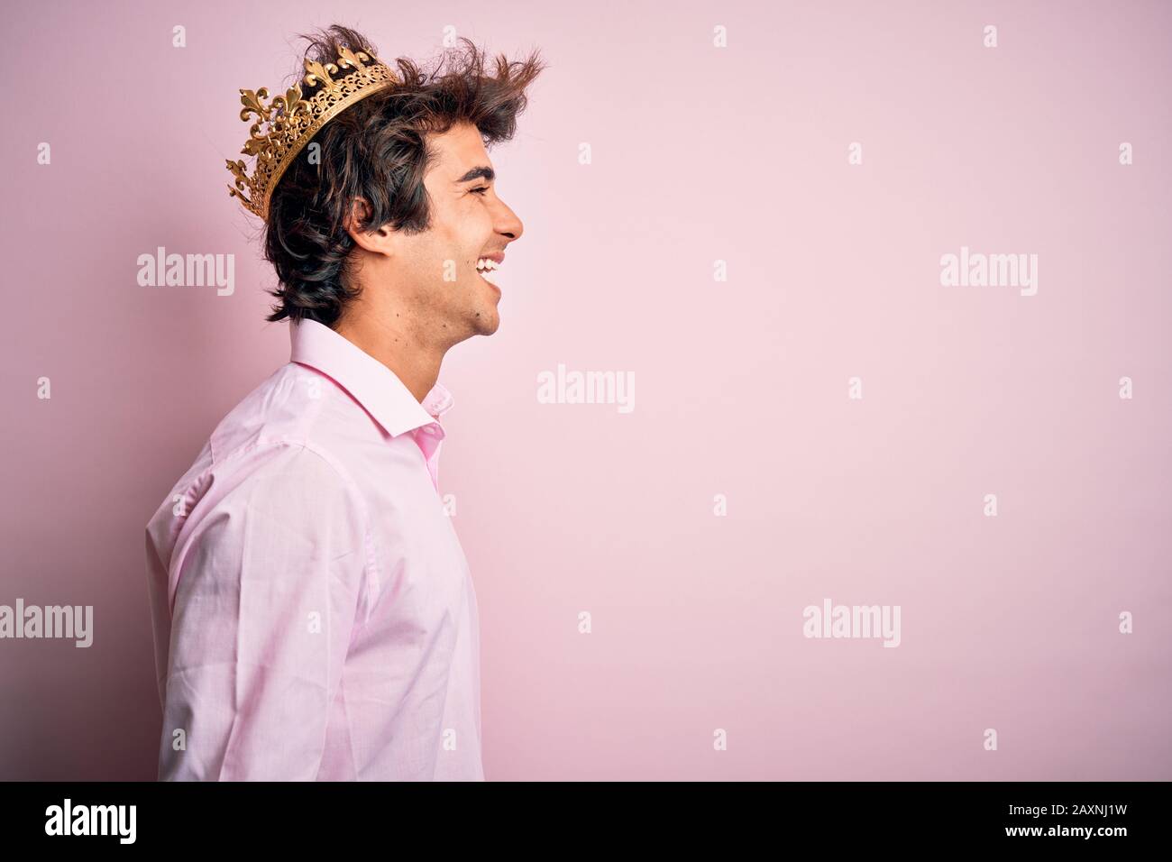 Young handsome man wearing king crown standing over isolated pink ...