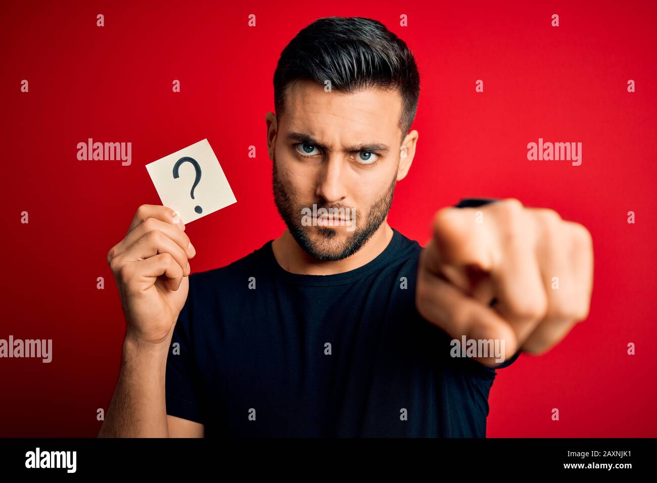Young handsome man holding paper with question mark symbol over red ...