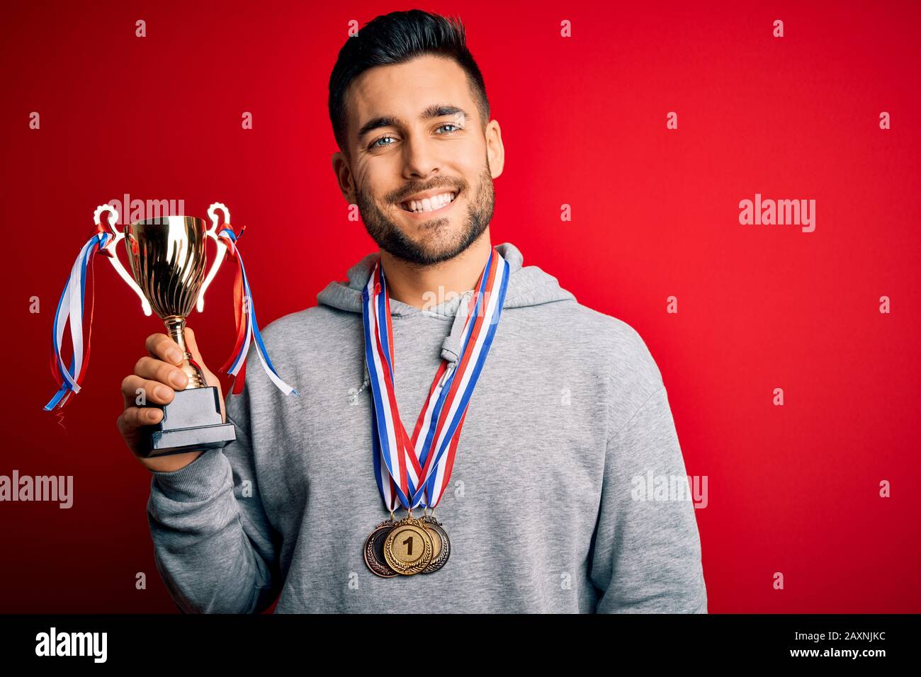 Young handsome succesful man holding trophy wearing medals over red ...