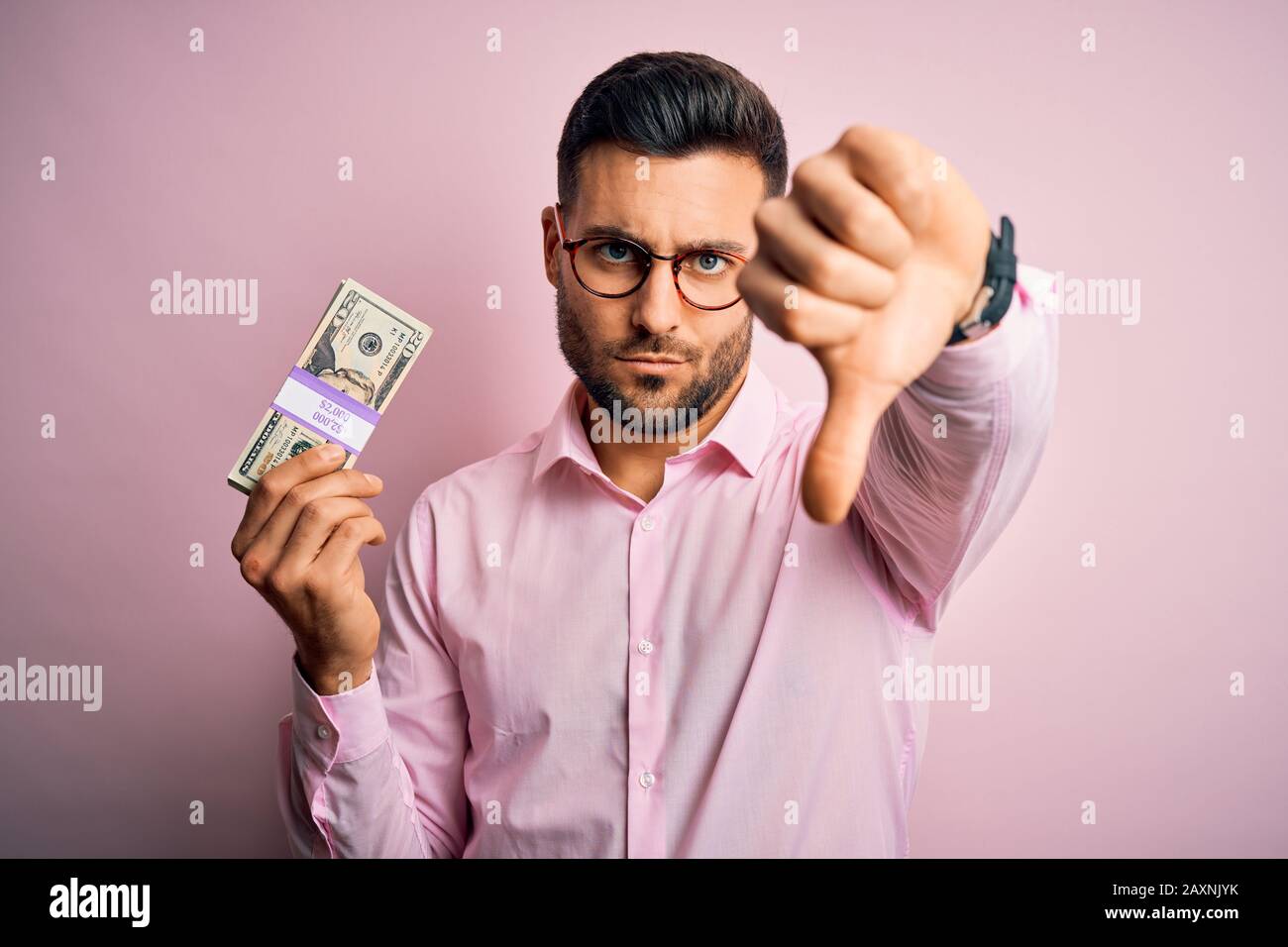 Young business man holding bunch of 20 dollars banknotes over pink ...