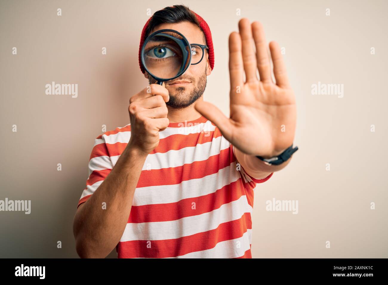 Young detective man looking through magnifying glass over isolated ...