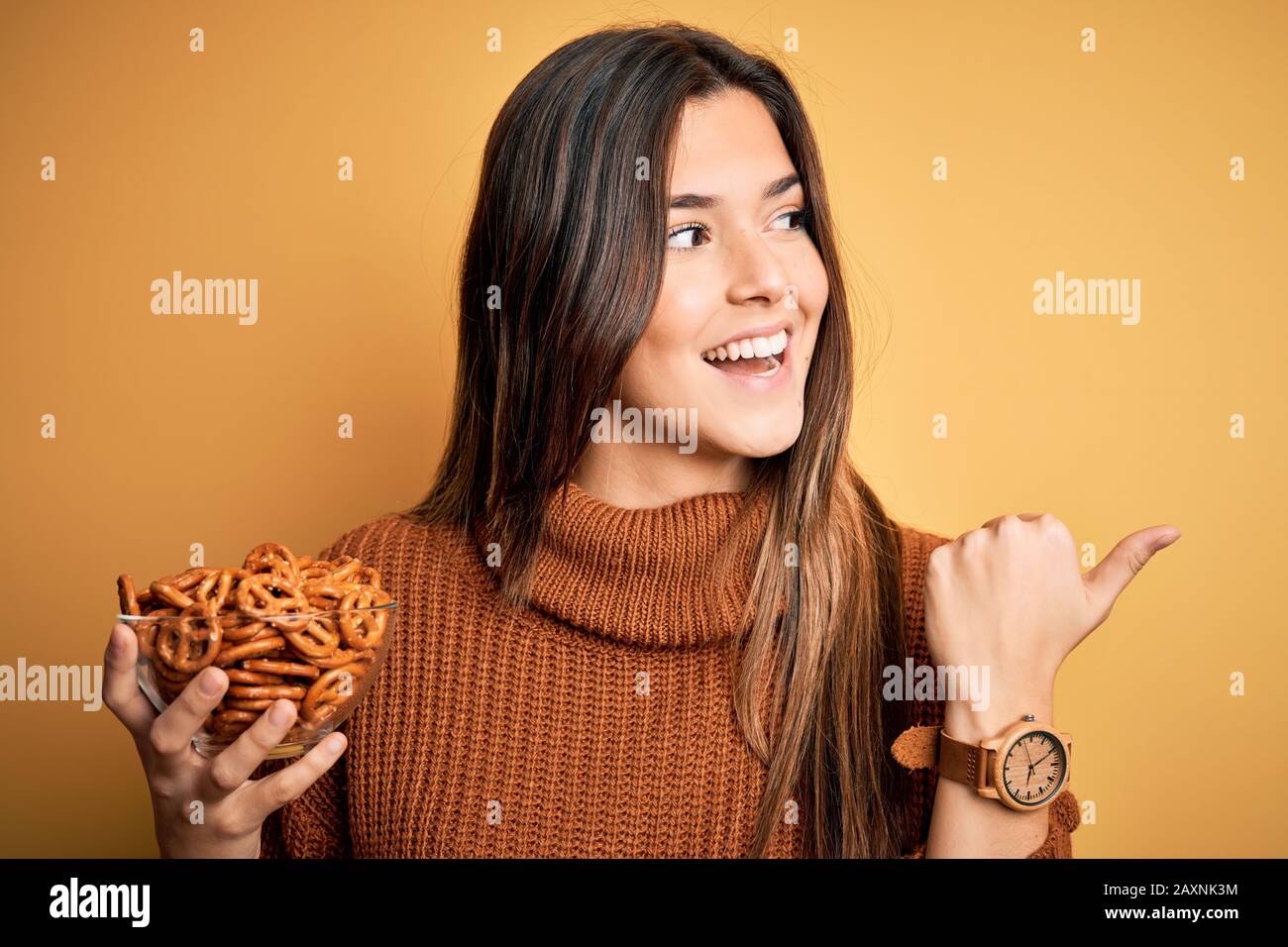 Young beautiful girl eating baked german pretzel standing over isolated ...