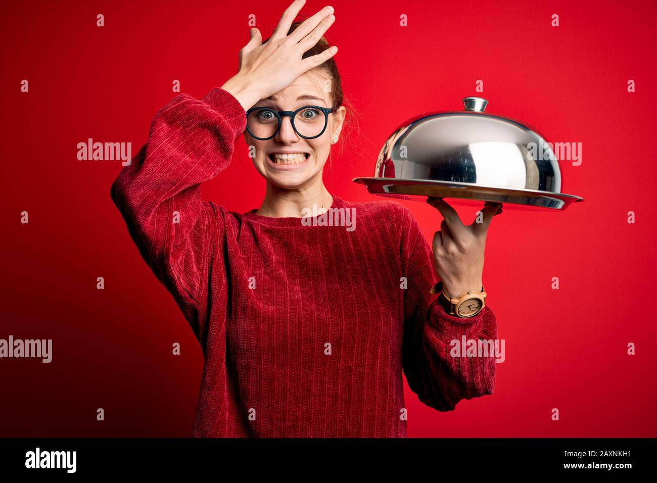 Young beautiful redhead woman holding waitress tray over isolated red ...